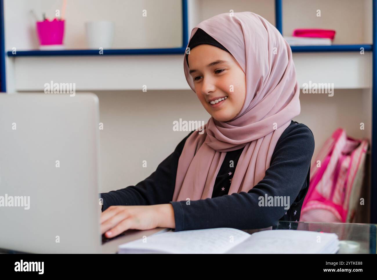 Portrait of a happy female Muslim student in hijab sitting at a desk ...