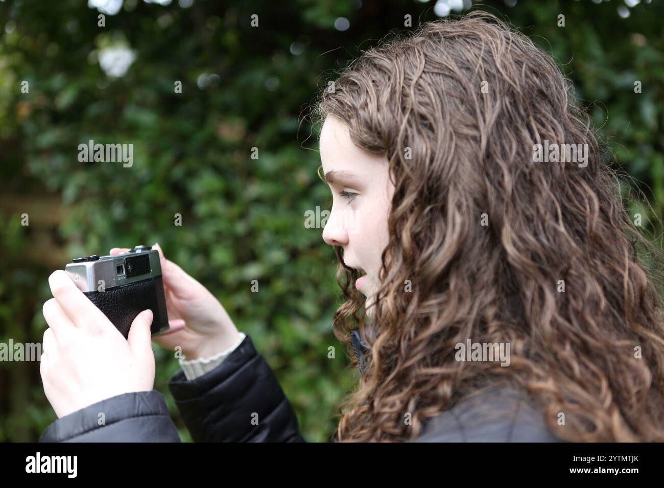 Teenage girl using a 35mm film camera analogue retro camera in garden ...