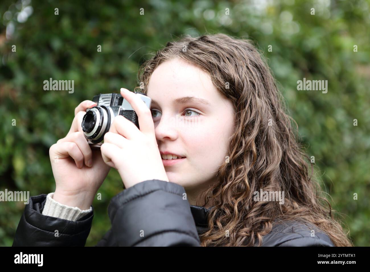 Teenage girl using a 35mm film camera analogue retro camera in garden ...