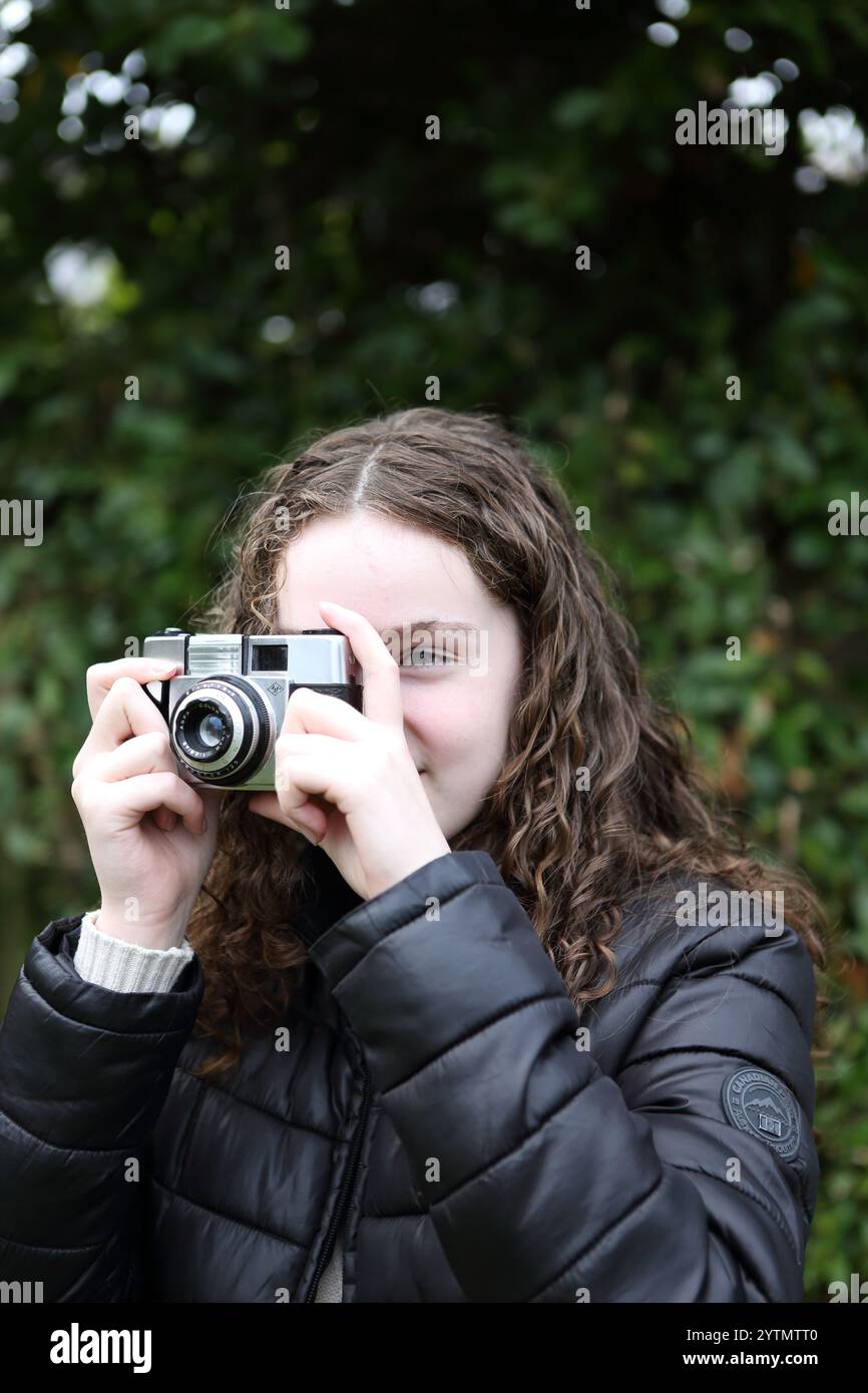 Teenage girl using a 35mm film camera analogue retro camera in garden ...