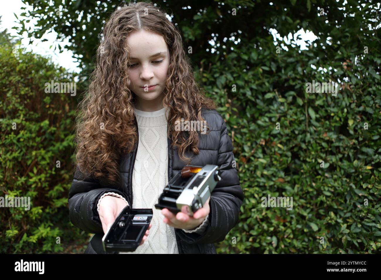 Teenage girl using a 35mm film camera analogue retro camera in garden ...