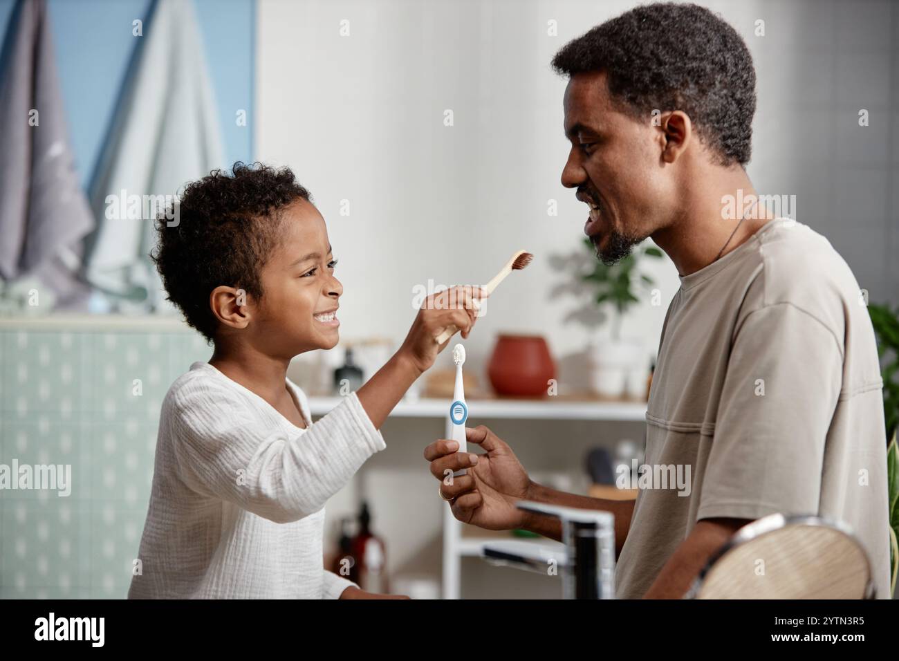 Side view of playful little Black boy brushing fathers teeth while ...