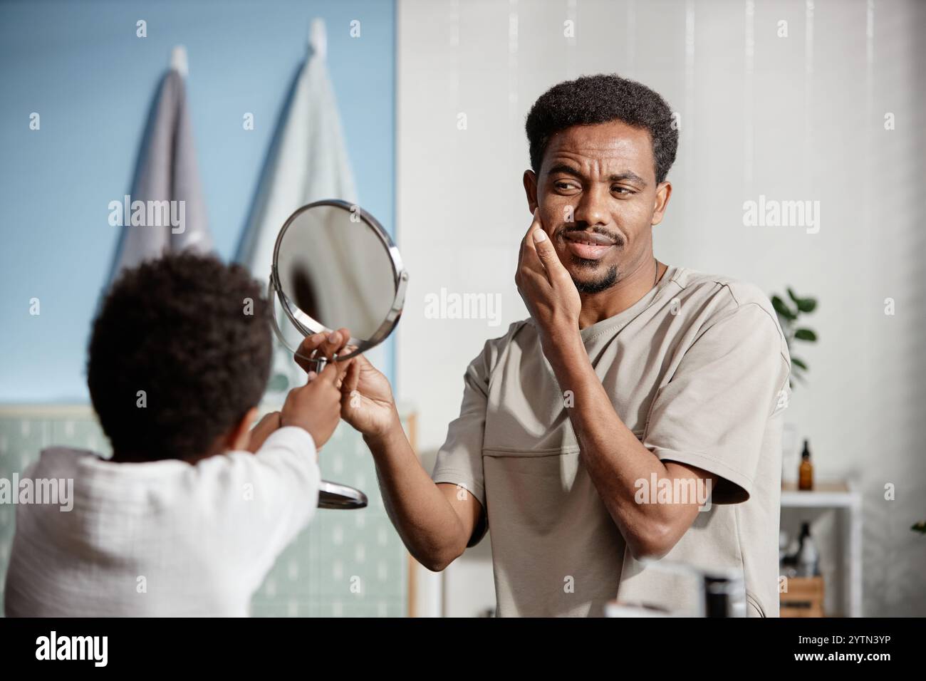 Medium shot of handsome Black man looking at reflection in mirror while ...