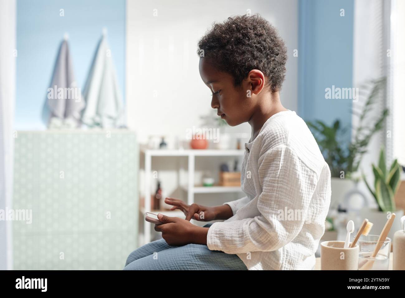 Side view of little African American boy tapping smartphone screen ...