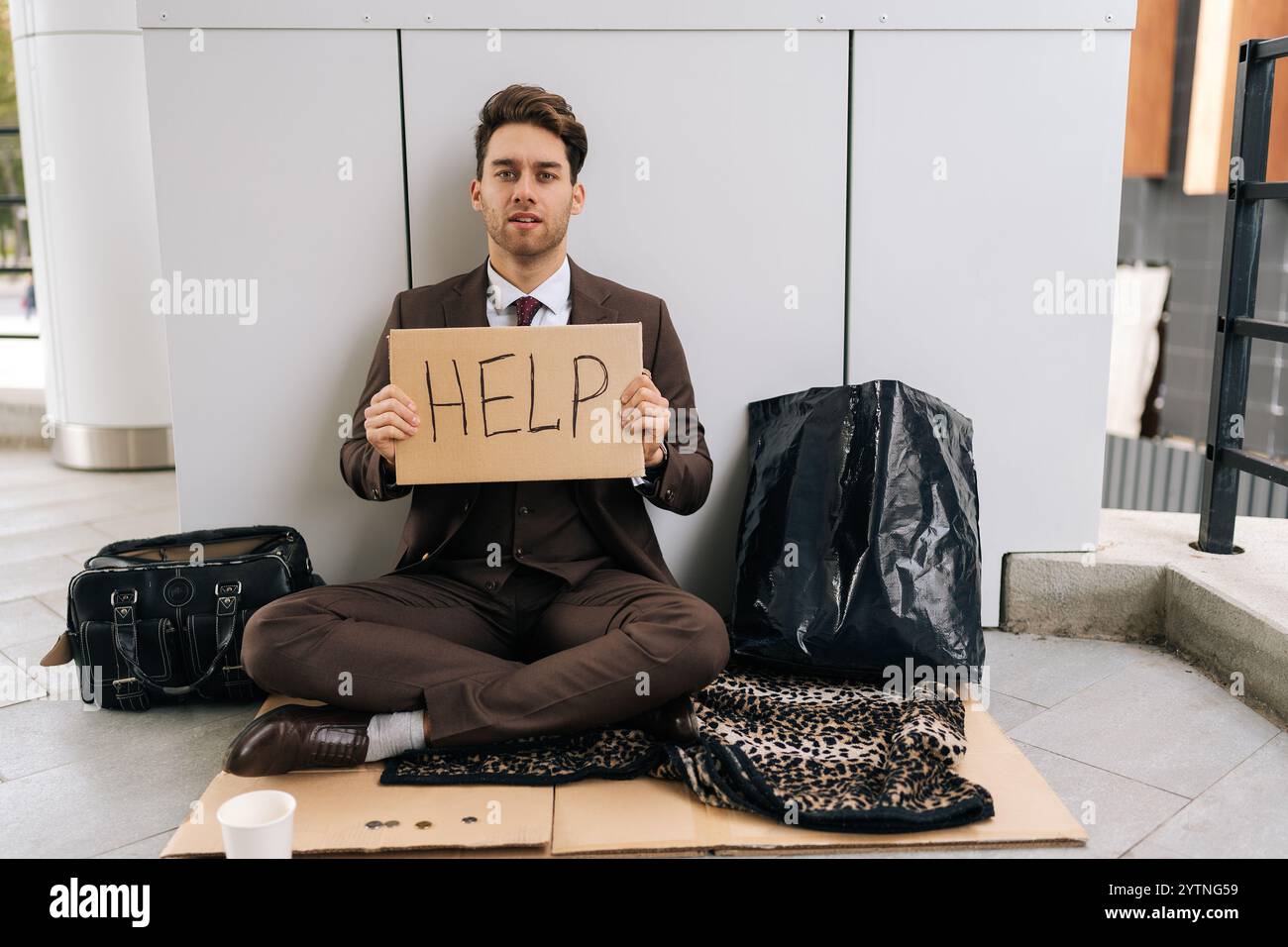 Front view of pensive homeless young business man in suit sitting on ...