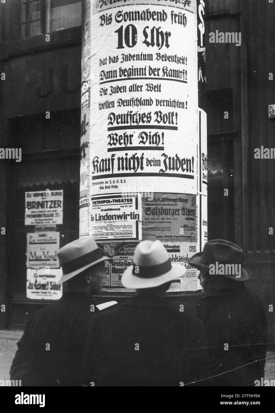 Berlin, April, 1933. Three men in front of a billboard with a poster ...