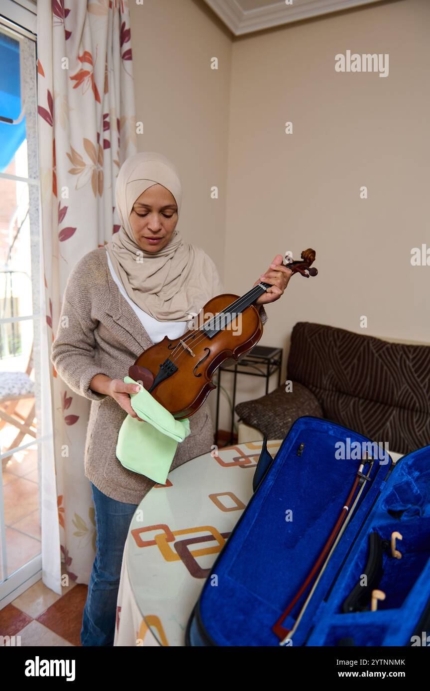 A woman in a cozy home setting prepares her violin with care, near a ...