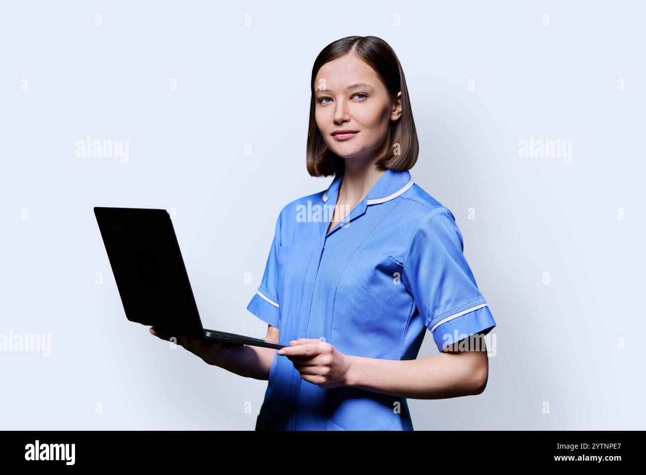 Female nurse with laptop, looking at camera on white studio background ...