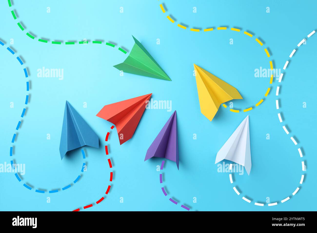 Colorful paper planes with flight paths on light blue background ...
