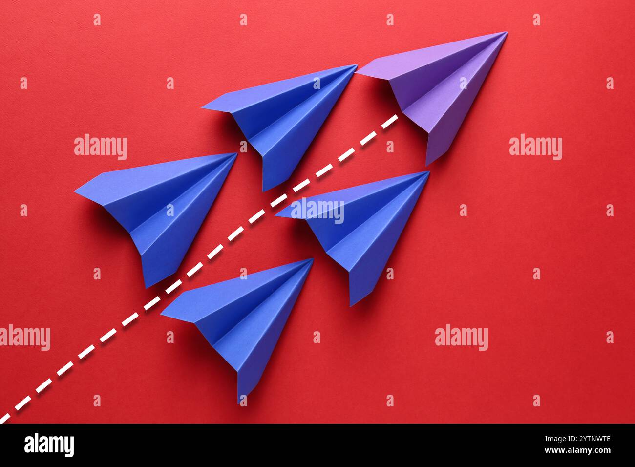 Purple paper plane with flight path among blue ones on red background ...