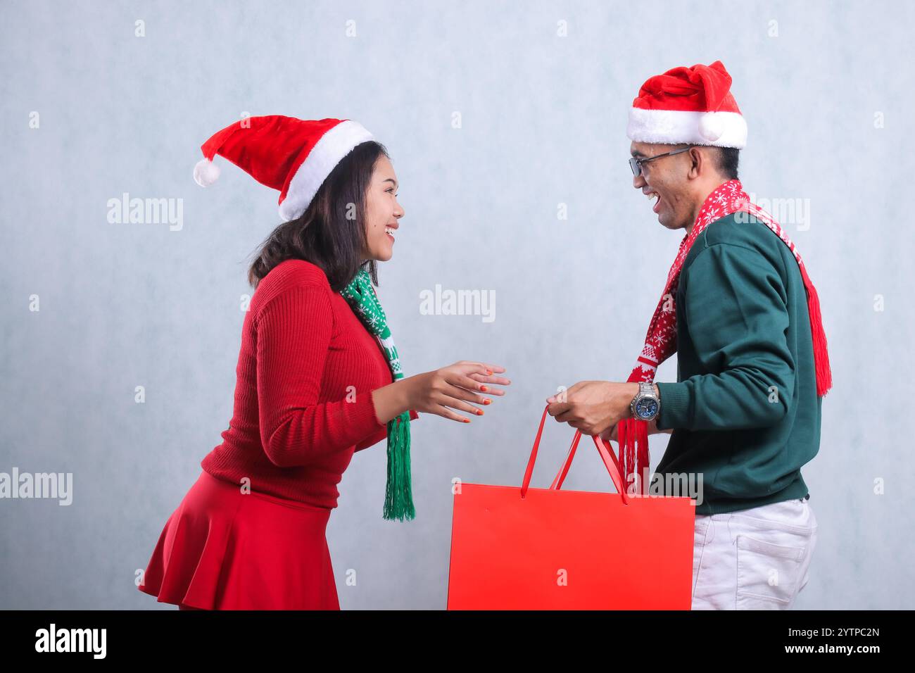 two young men wearing Christmas sweaters, Santa hats and scarves ...