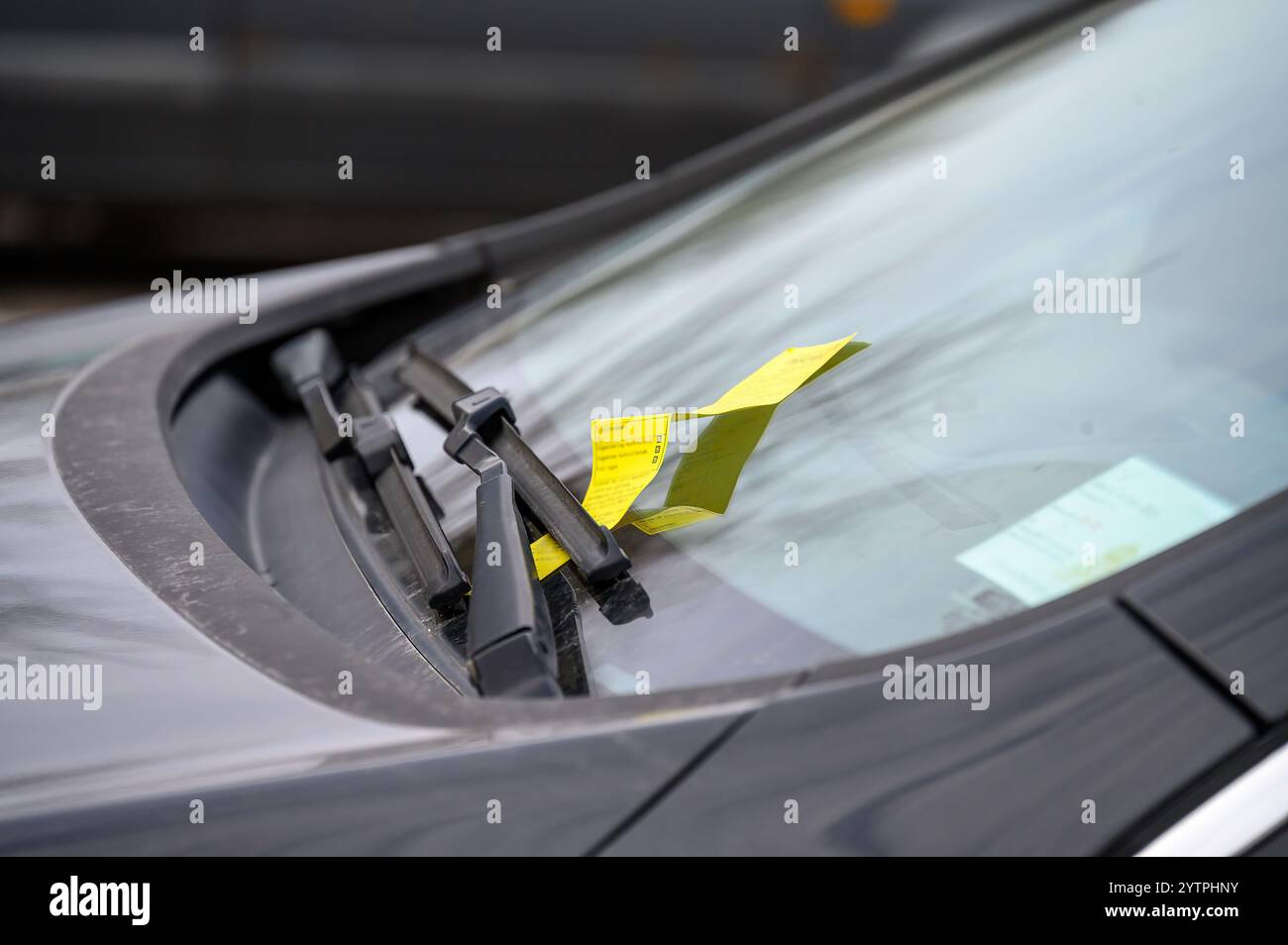 A bright yellow parking ticket is placed on the windshield of a parked ...
