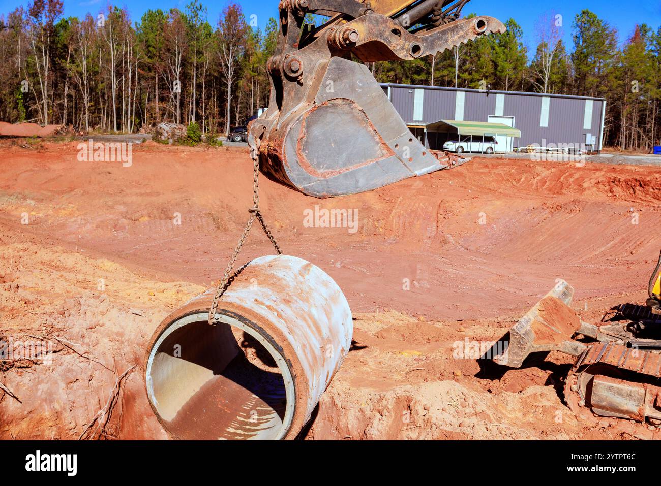 Excavator carefully lowers concrete pipe into freshly dug trench at ...