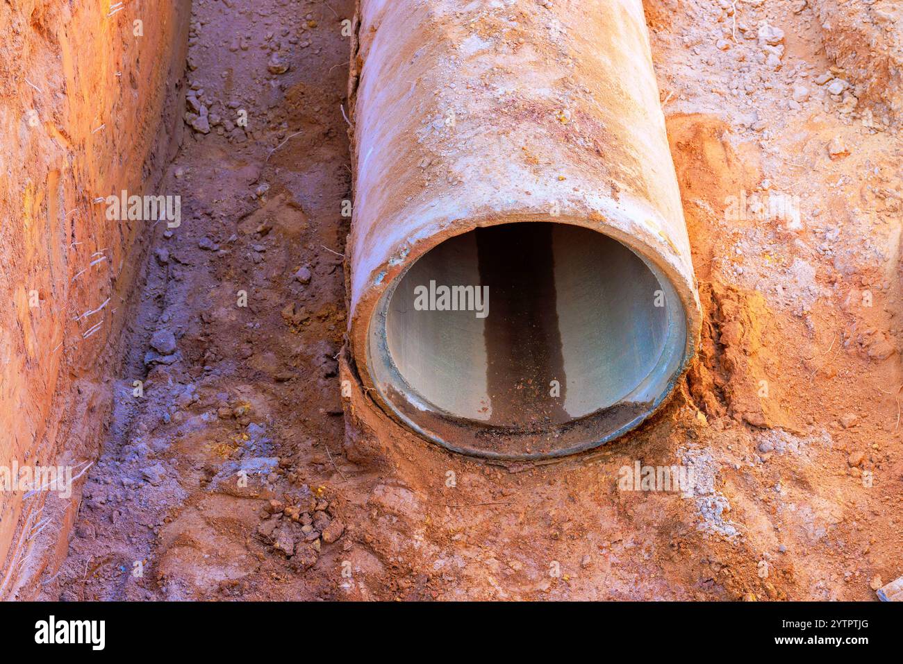 Exposed concrete pipe rests in dirt, surrounded by soil, gravel at ...