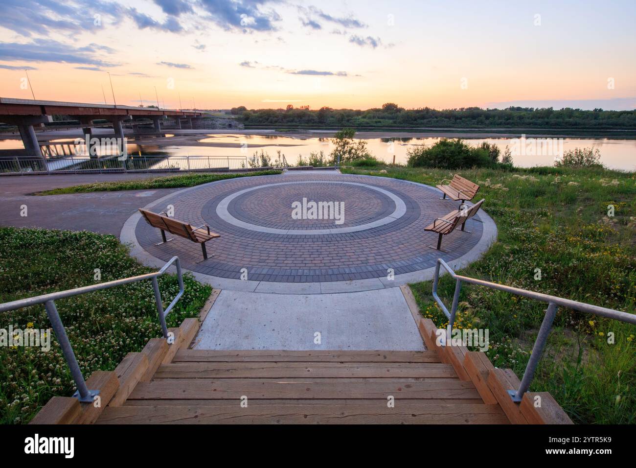 A circular paved area with benches and a bridge in the background. The ...