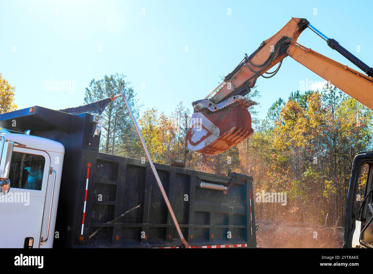 Large excavator lifts bucket of materials over dump truck at ...