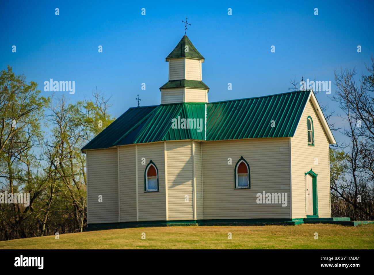 A small white church with a green roof and a green cross on top. The ...