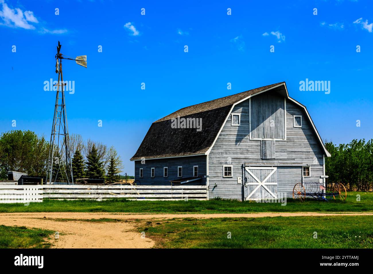 A large, old barn with a windmill on top of it. The barn is surrounded ...