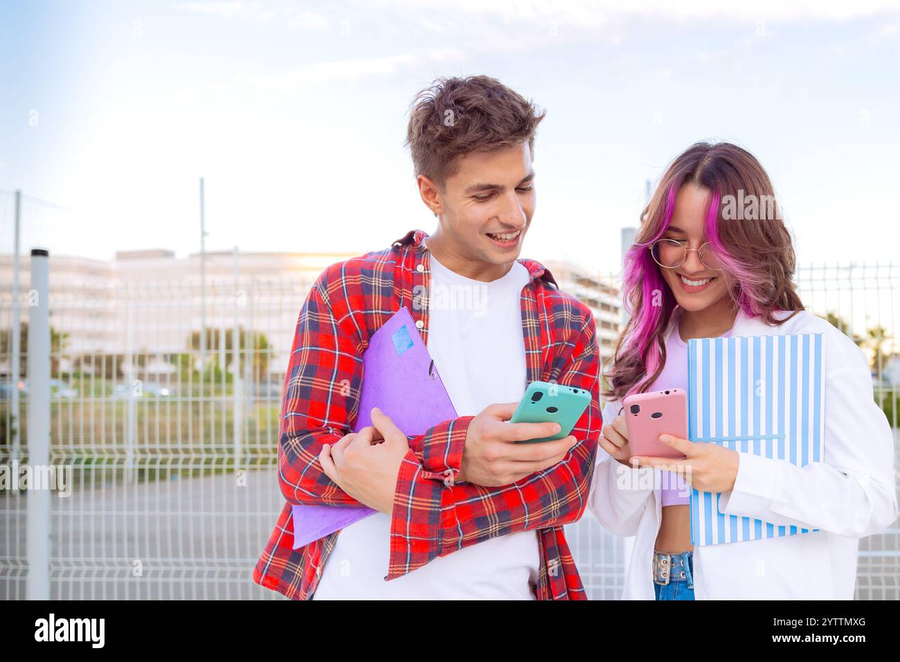 Two students smiling and using smartphones outdoors Stock Photo - Alamy