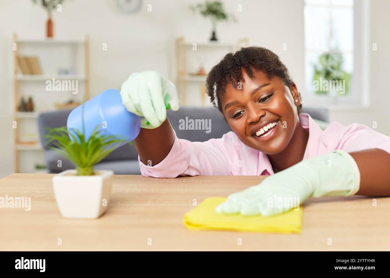 Happy african american maid polishing table with yellow napkin, close ...