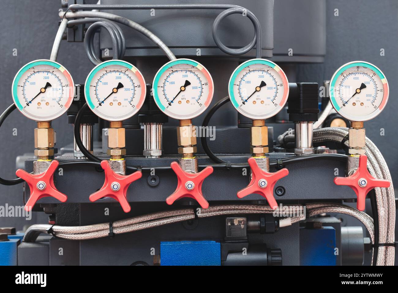 A group of valves with red handles are connected to a machine. The ...