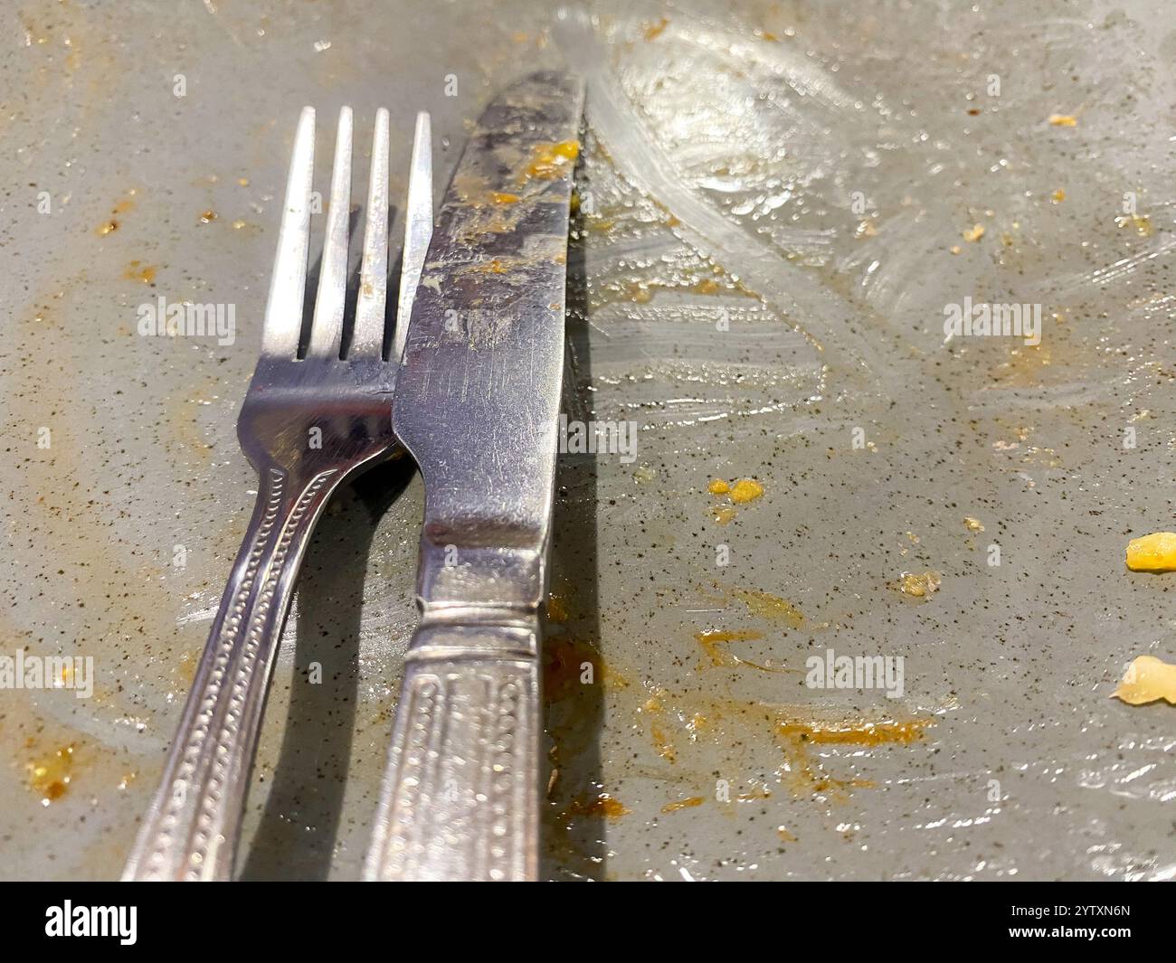 A knife and fork on a greasy plate at the end of a meal Stock Photo - Alamy