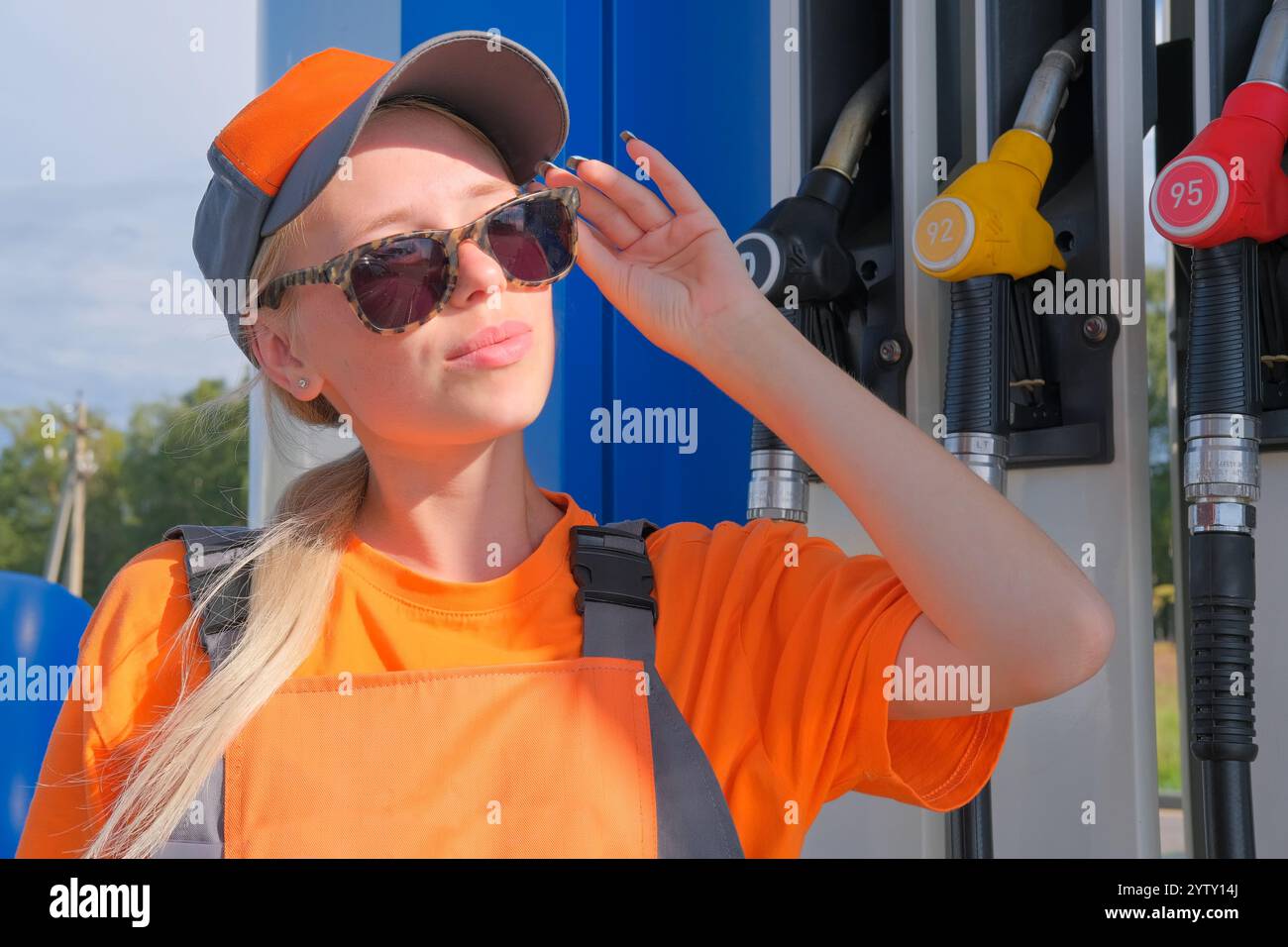 Young blonde woman, female gas station attendant worker wearing orange ...