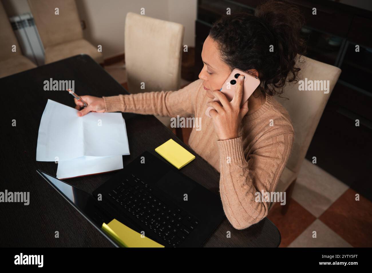 A woman efficiently manages her tasks by handling paperwork, a phone ...