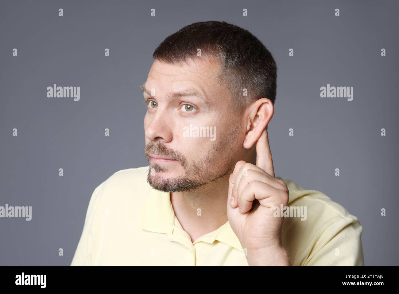 Man showing hand to ear gesture on grey background Stock Photo - Alamy