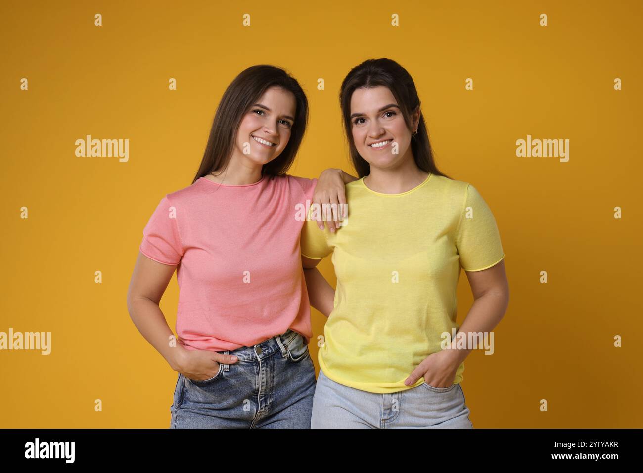 Portrait of happy twin sisters on orange background Stock Photo - Alamy