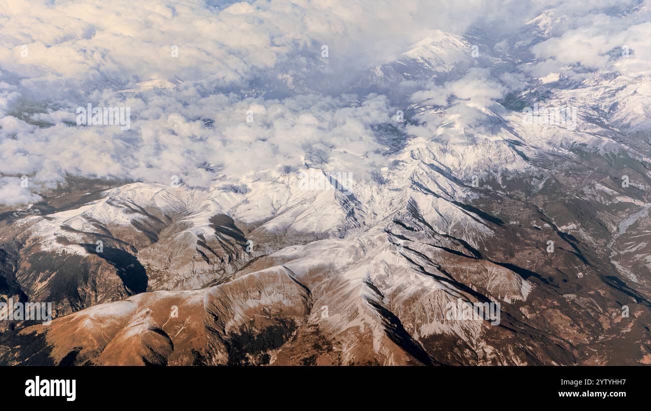 Above the peaks with clouds, capped Alps with rugged mountain peaks extending across the ...