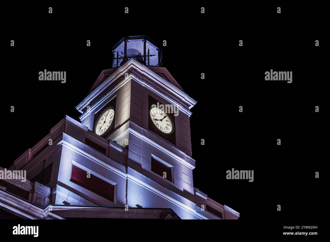 A clock tower with two clocks on it. The clocks are lit up in blue. The ...