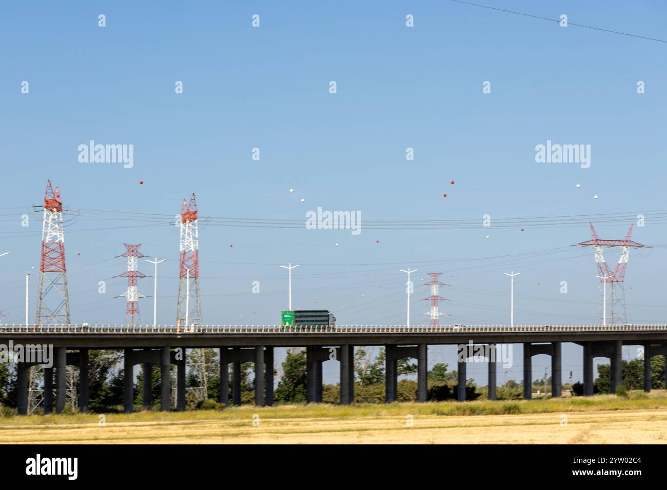 Green semi truck driving on highway overpass near tall power lines and ...