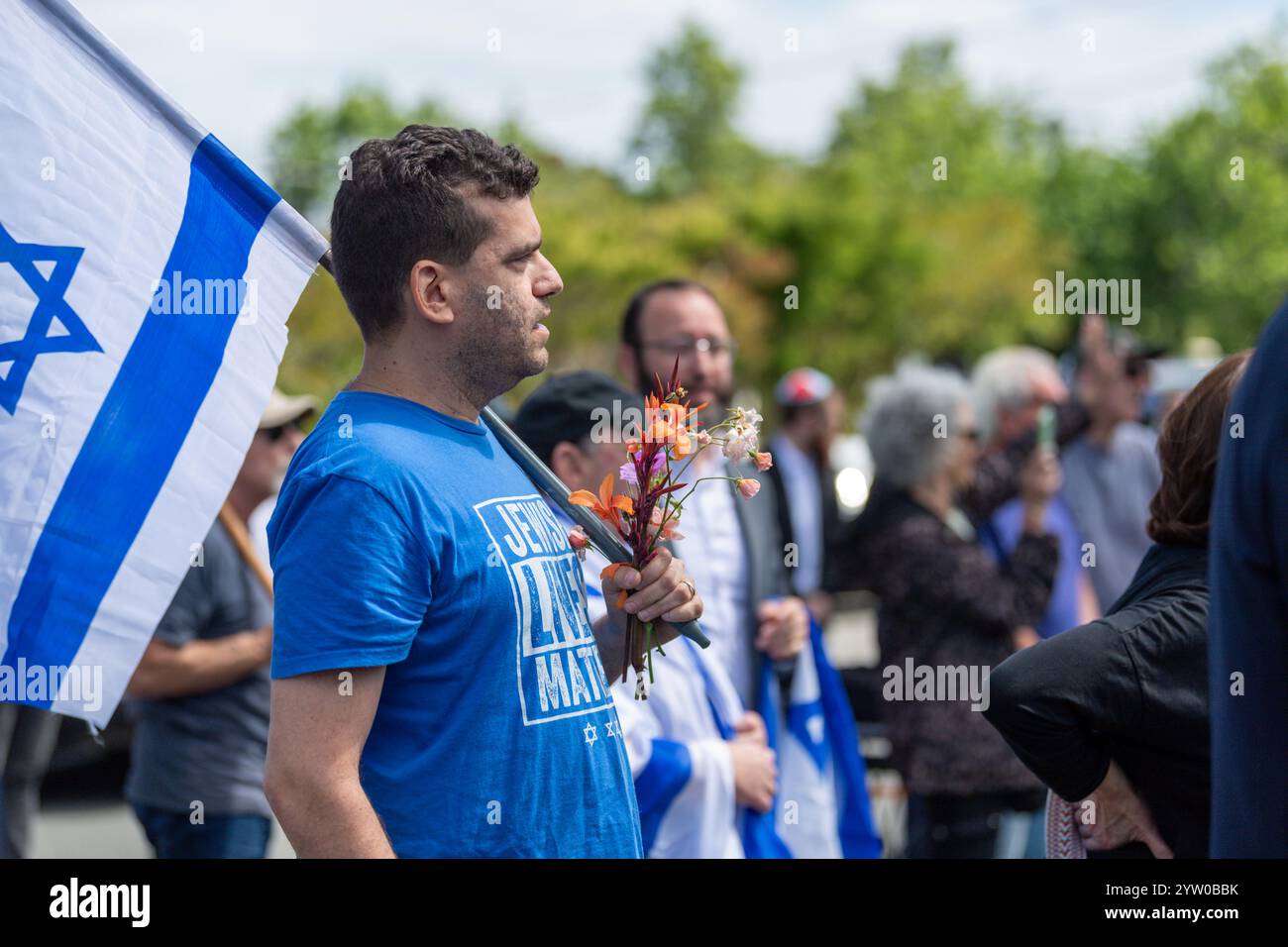 A man holds flowers to leave at the Synagogue as protesters hold signs ...