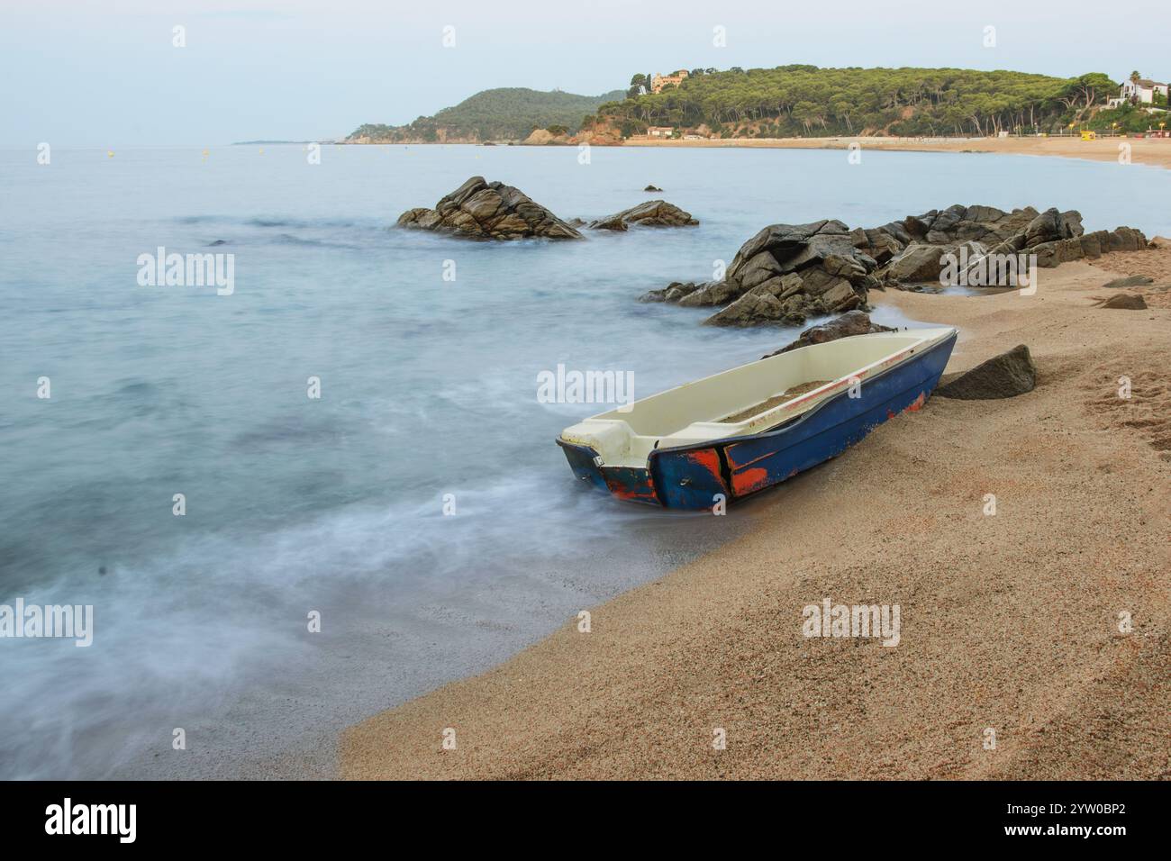 An old, weathered boat sits abandoned on a sandy beach, waves gently ...