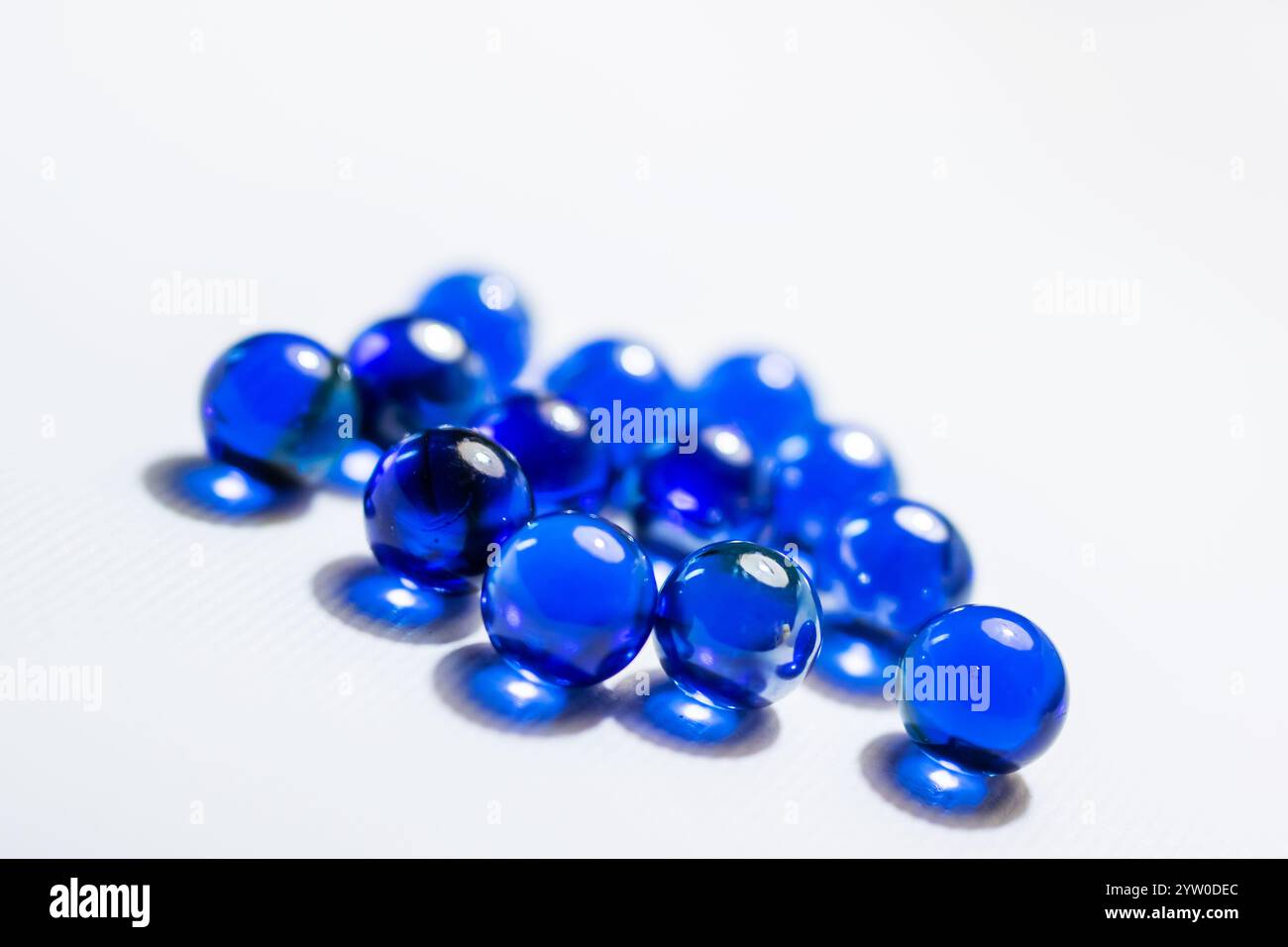 A collection of vibrant blue marbles is displayed on a clean, white ...
