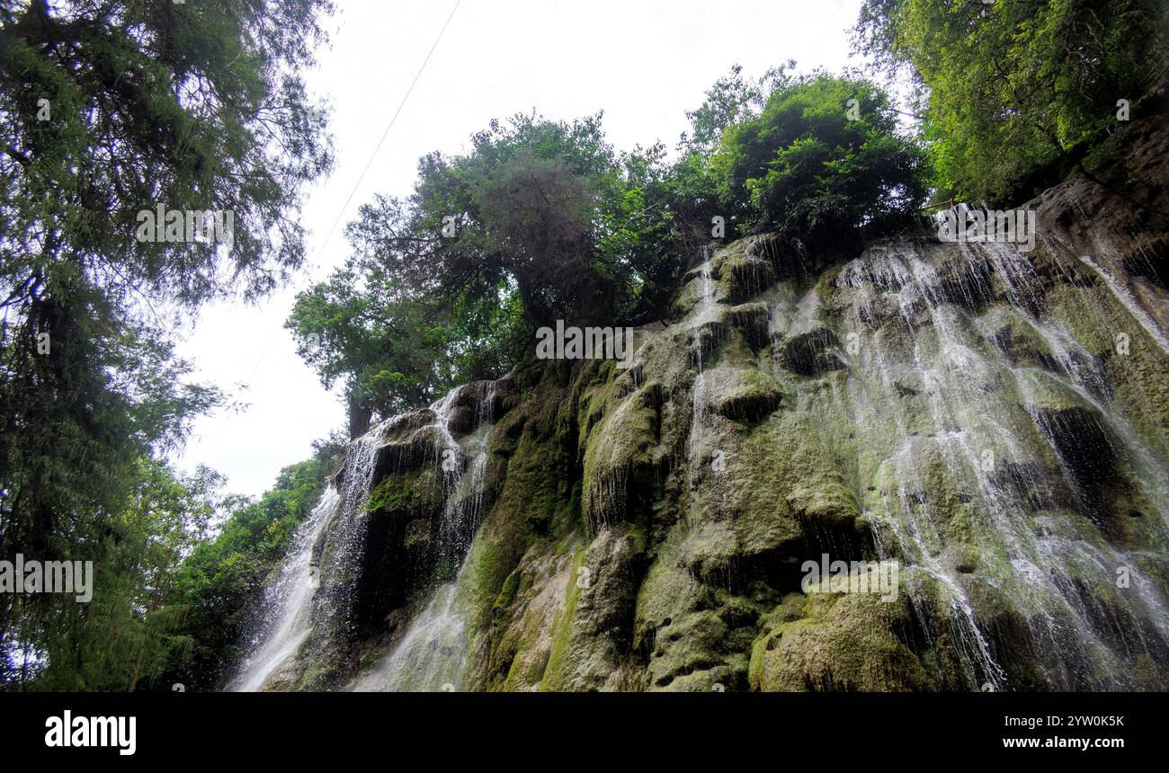 A stunning waterfall flows dramatically over a rugged cliff face, with ...