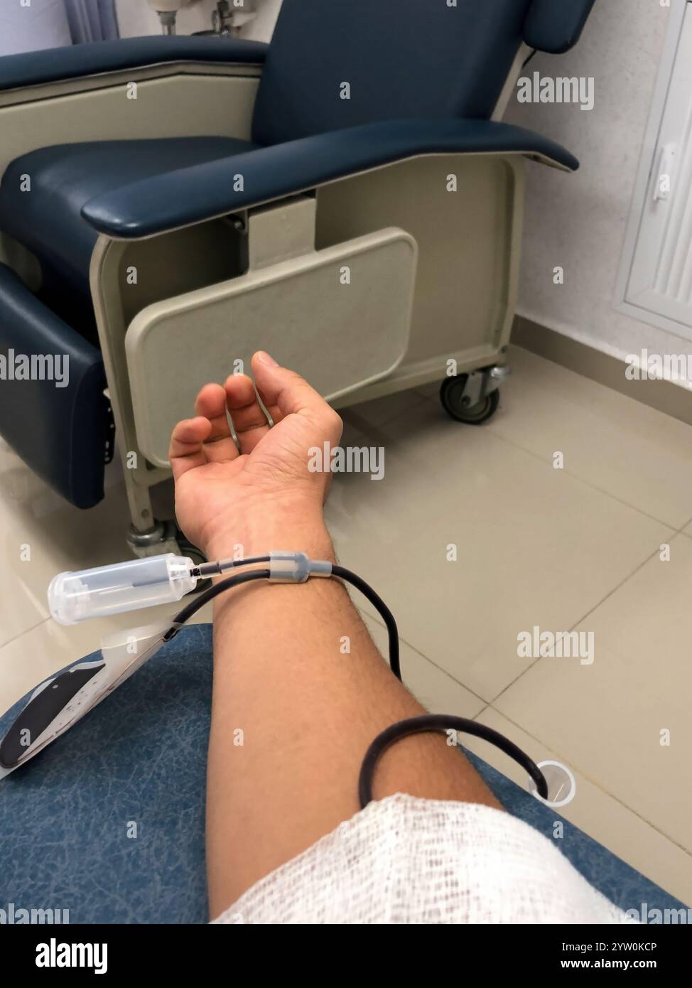 A person rests in a medical chair, wearing a hospital gown, as an intravenous line is attached ...