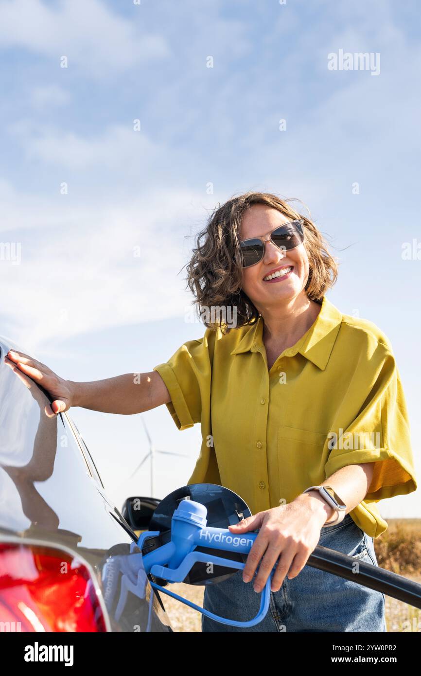 Woman with fueling hydrogen car. Refueling car with hydrogen fuel. Wind ...