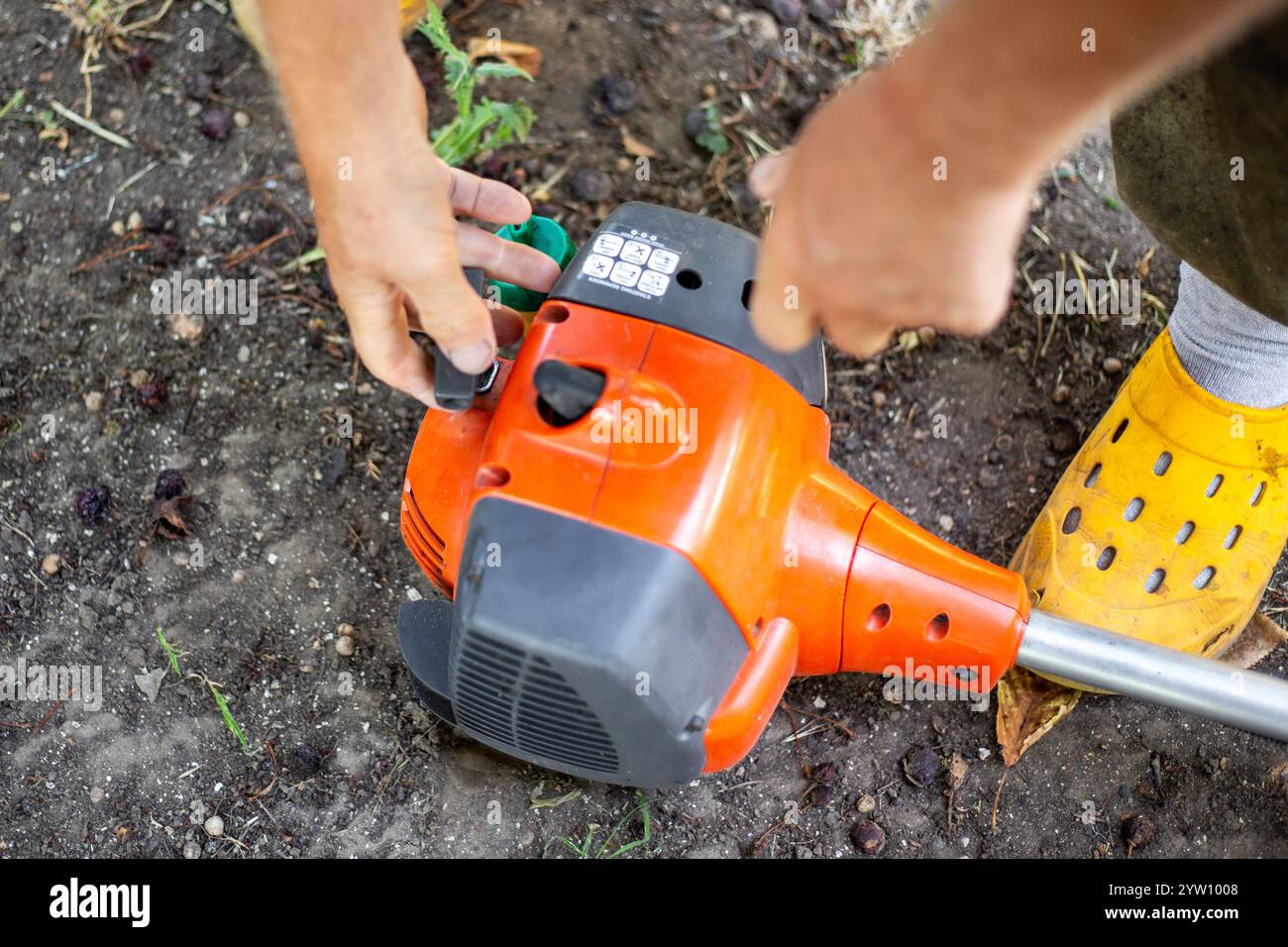 Starting a gas mower to cut grass. A man pulls the recoil starter to ...