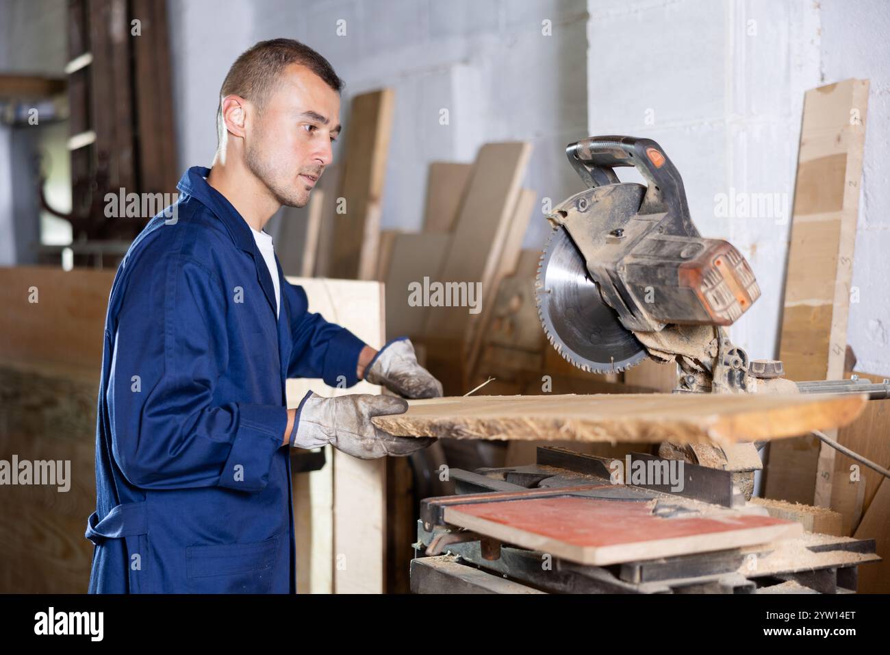 Working at sawmill - man saws wooden board using circular saw Stock ...