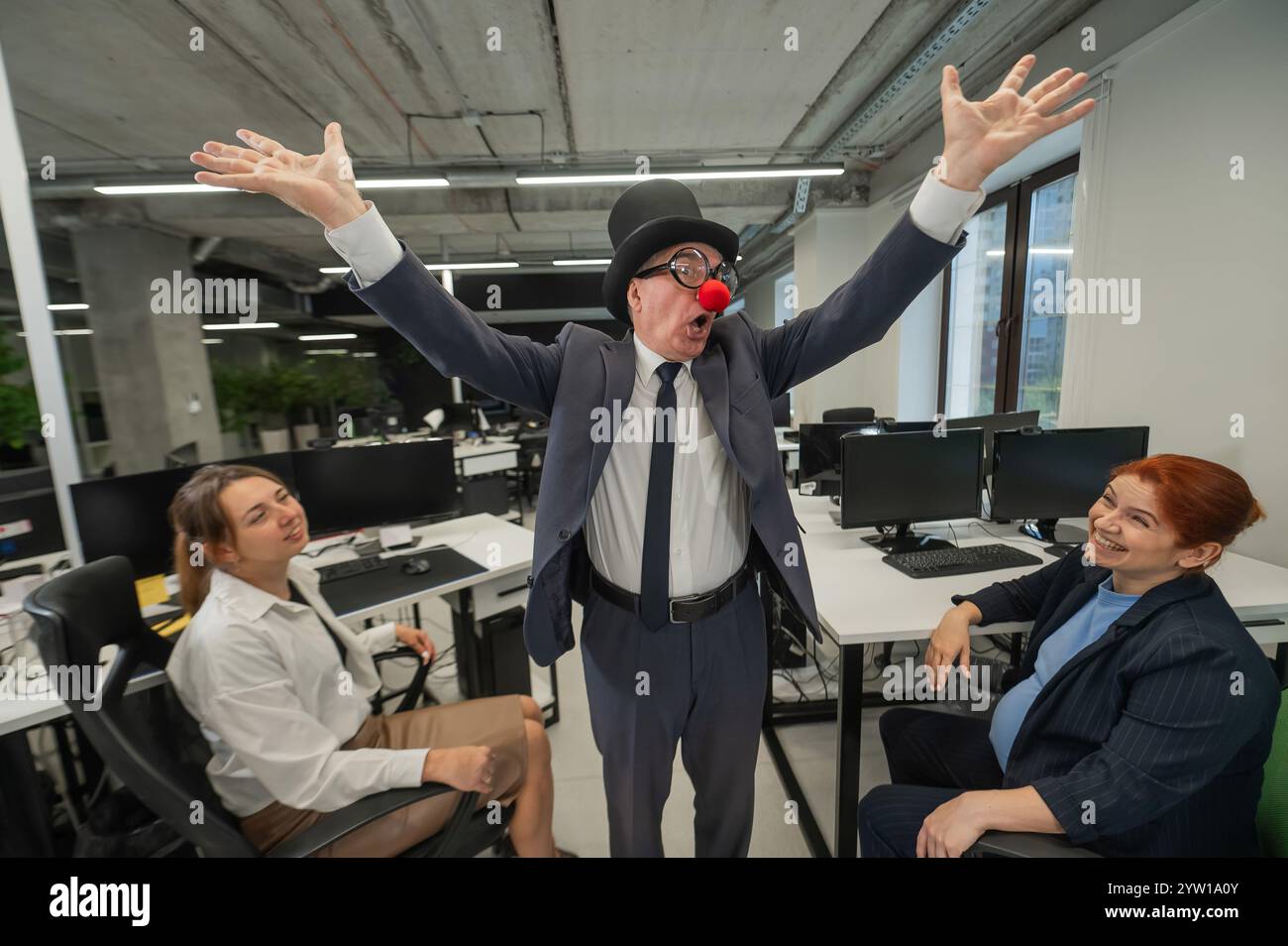 An elderly Caucasian man in a clown costume amuses two Caucasian women ...