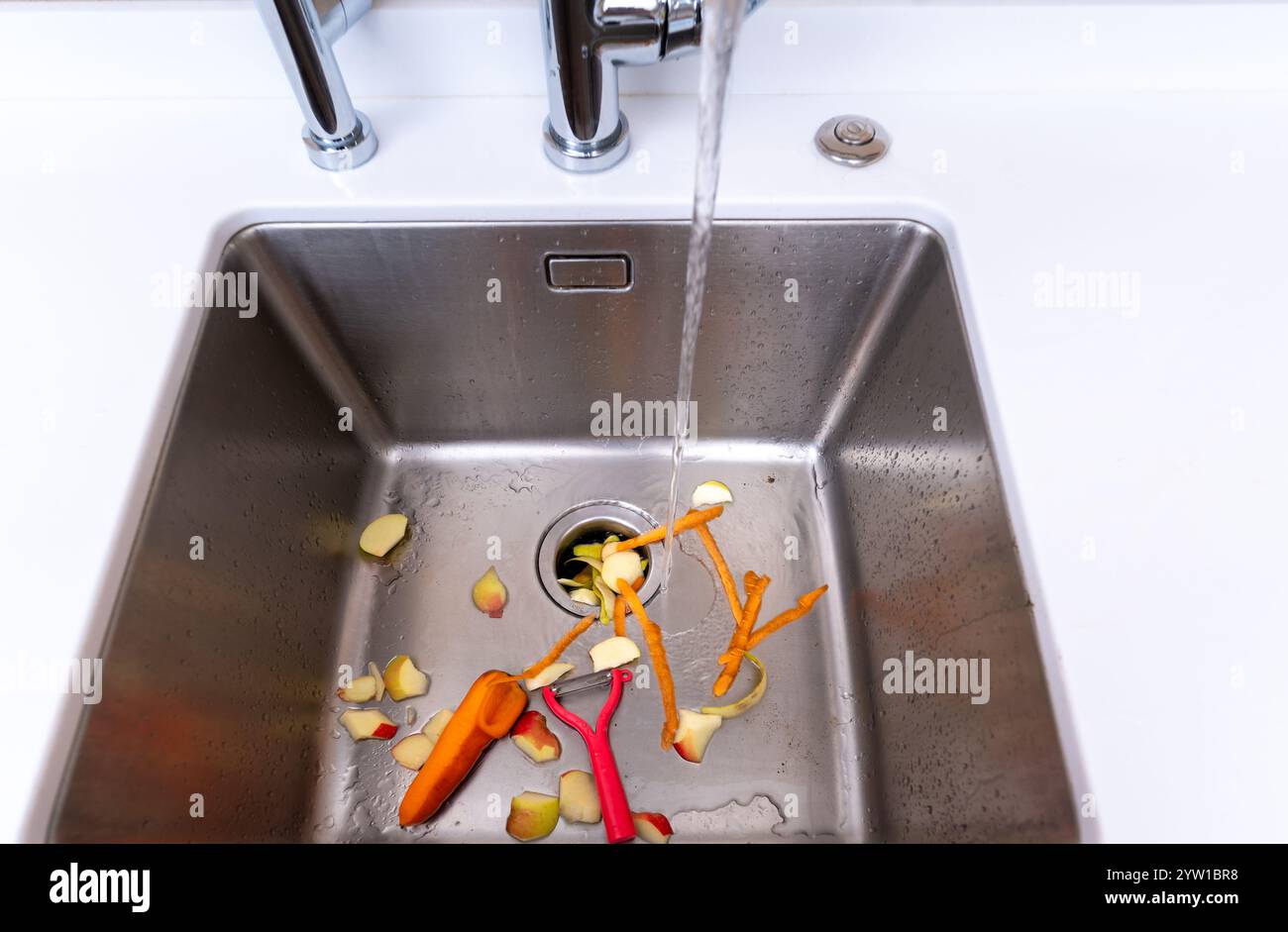 Kitchen sink with running water and vegetable peels during cleanup ...