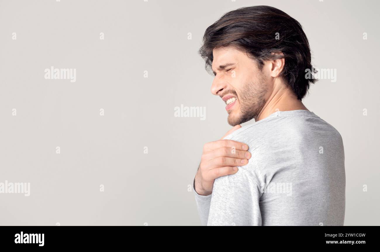 Man with painful expression, rubs shoulder with his hand Stock Photo ...