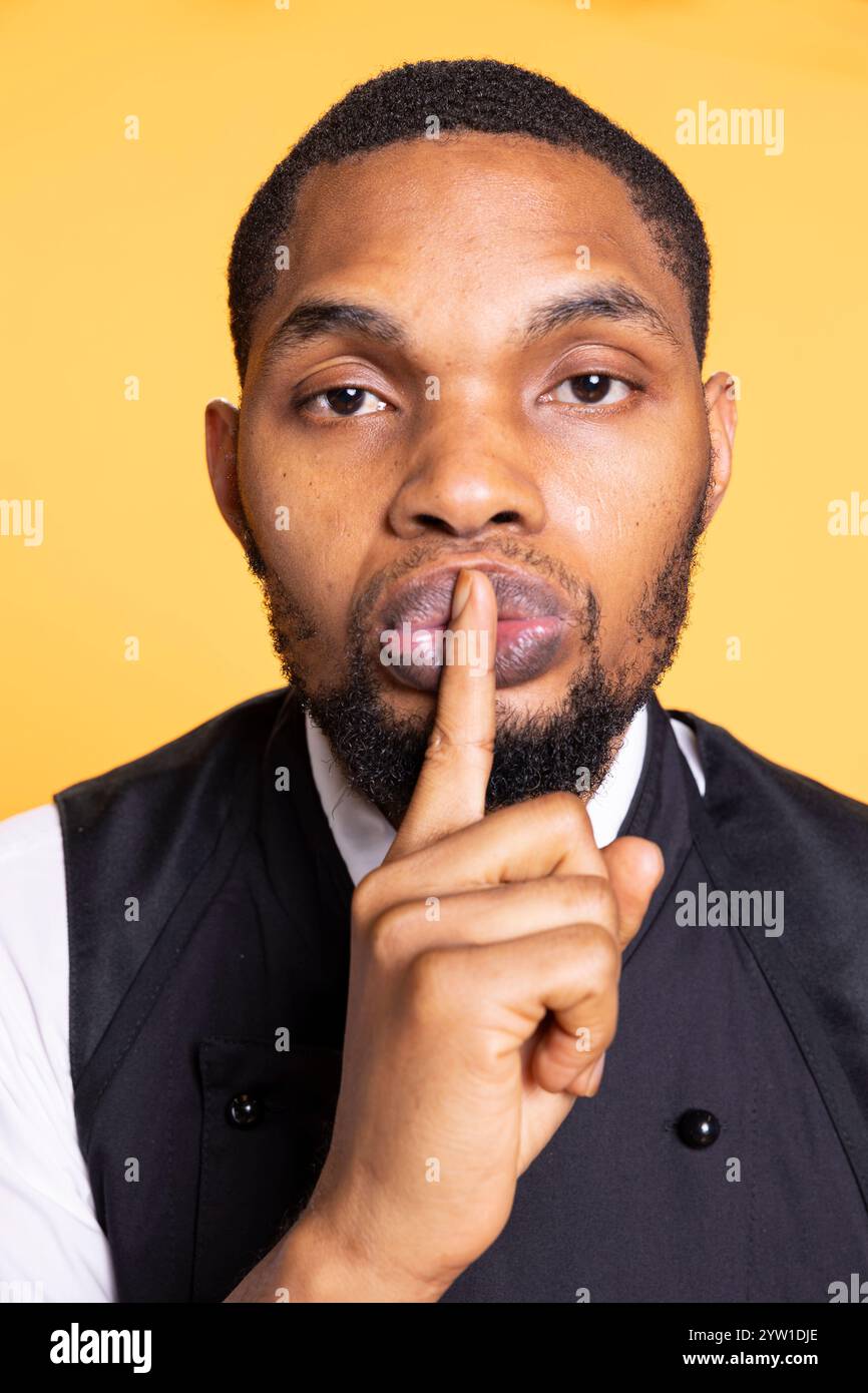 Restaurant waiter doing the hush mute gesture to be quiet and keep ...