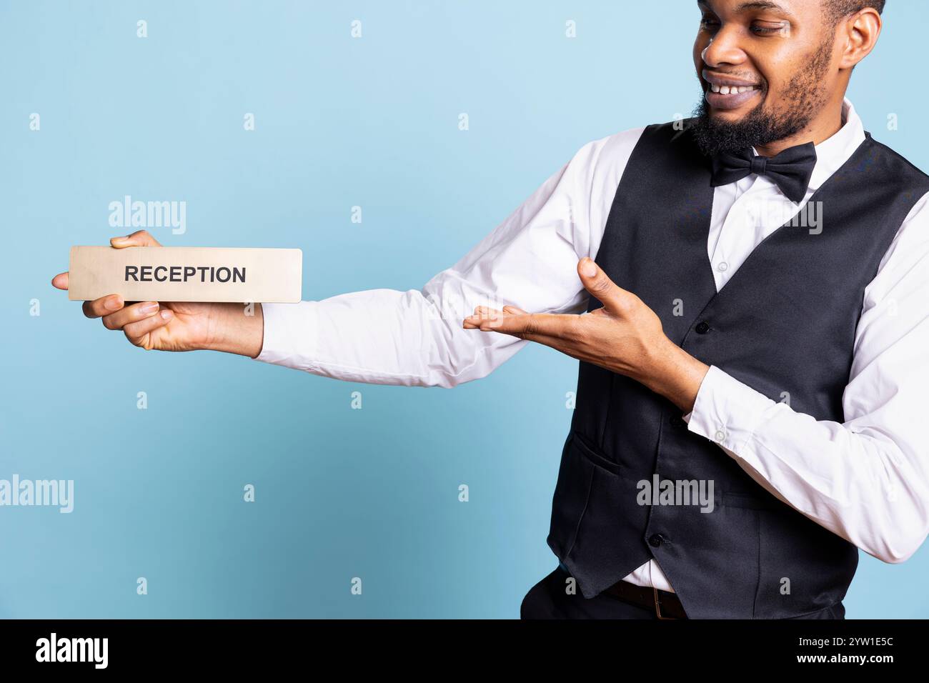 Young bellhop pointing at an indicator for the reception area front ...
