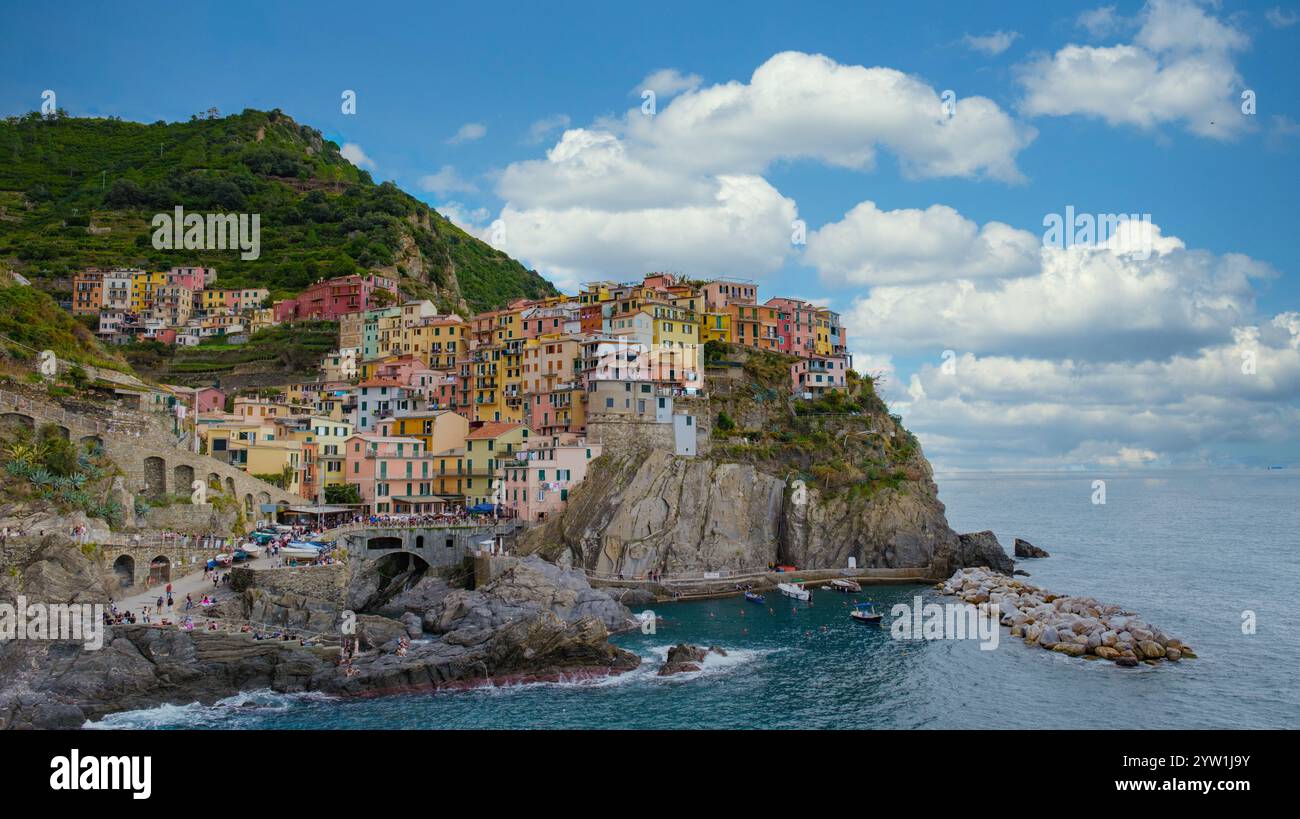 Wander through the vibrant streets of Manarola as the sun breaks through clouds, illuminating ...