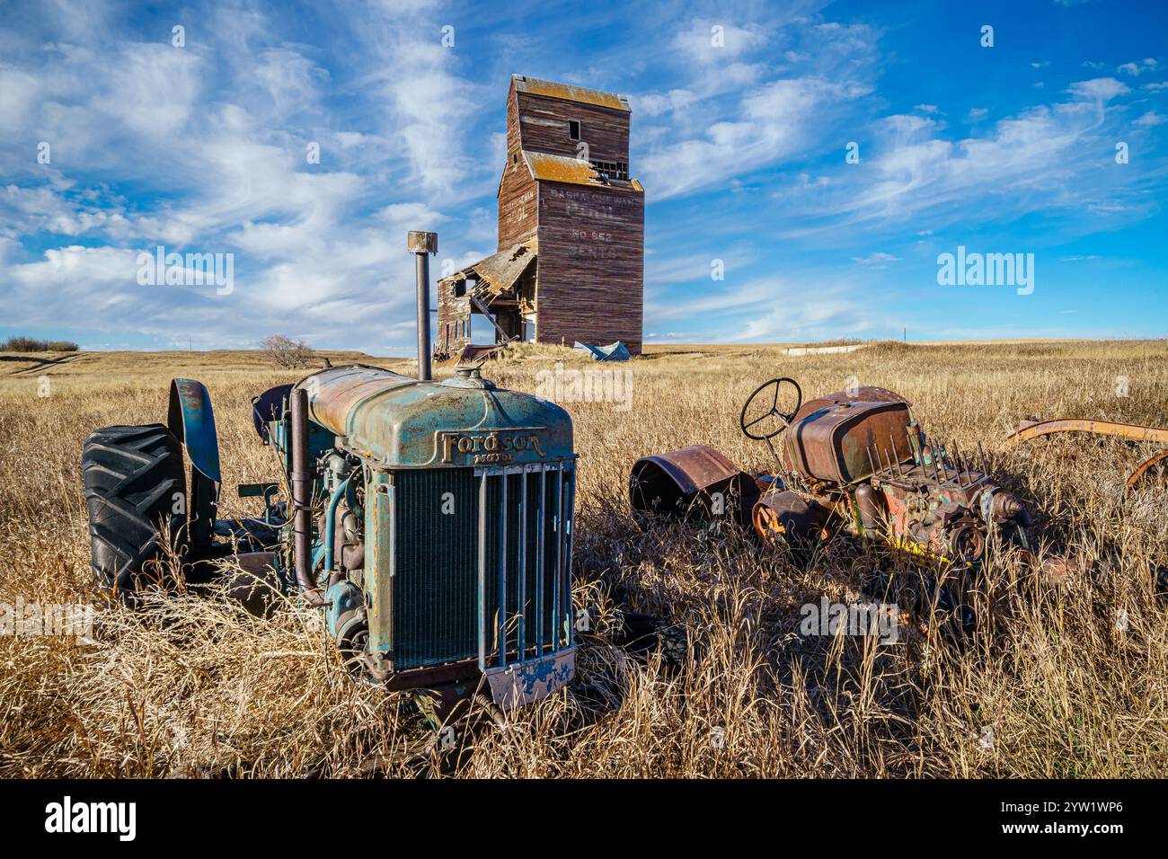 An old tractor is sitting in a field next to a grain elevator. The ...