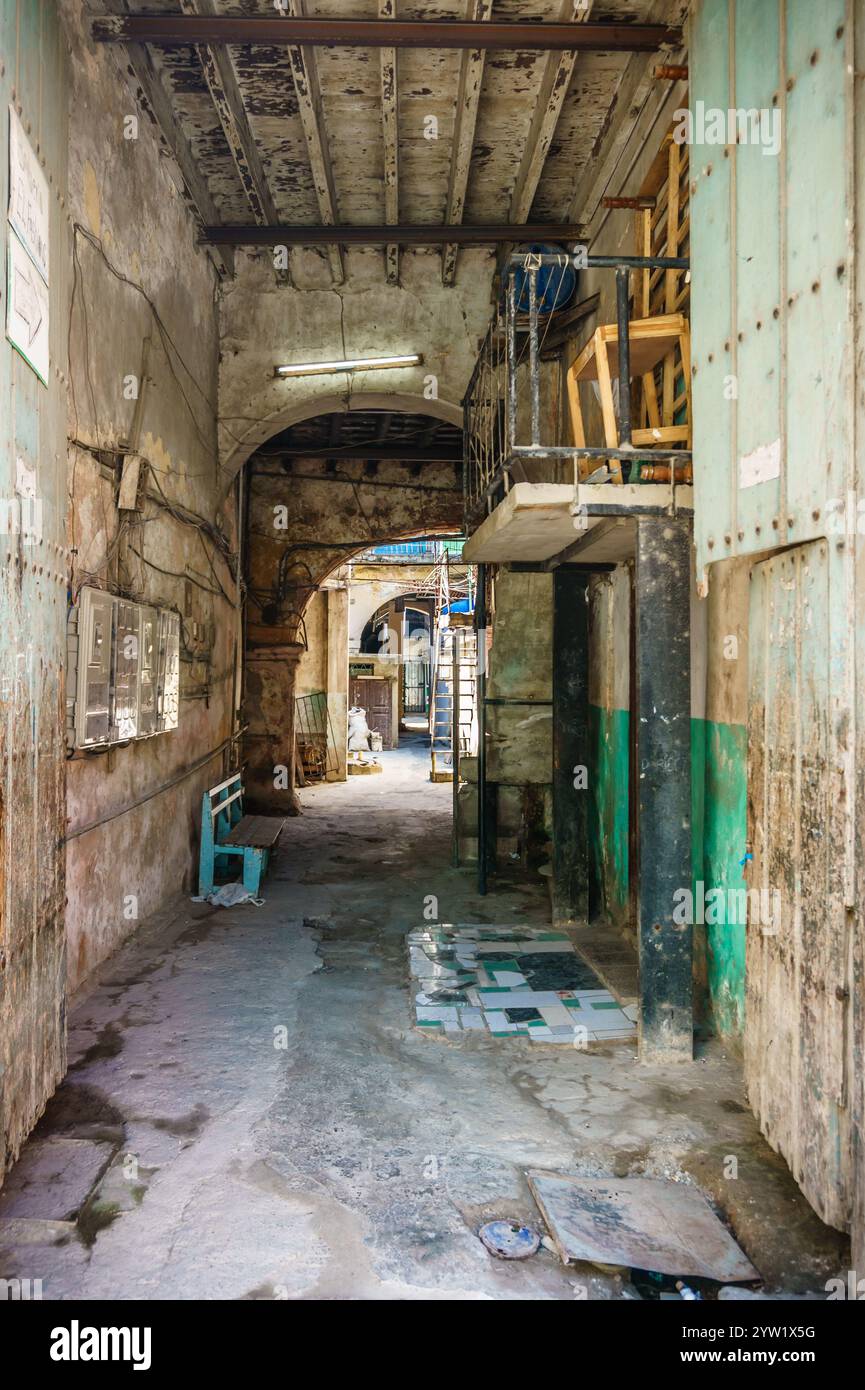 A narrow alleyway with a green and white wall. The wall has a few holes ...