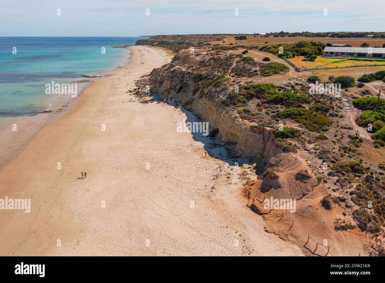 Aerail view of two small figures walking along a beach below rugged ...
